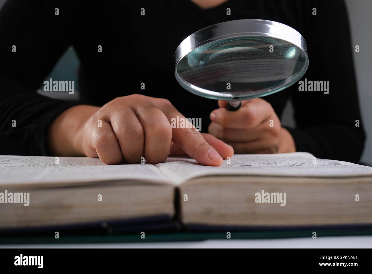 Close-up of a woman looking through a magnifying glass at a textbook ...