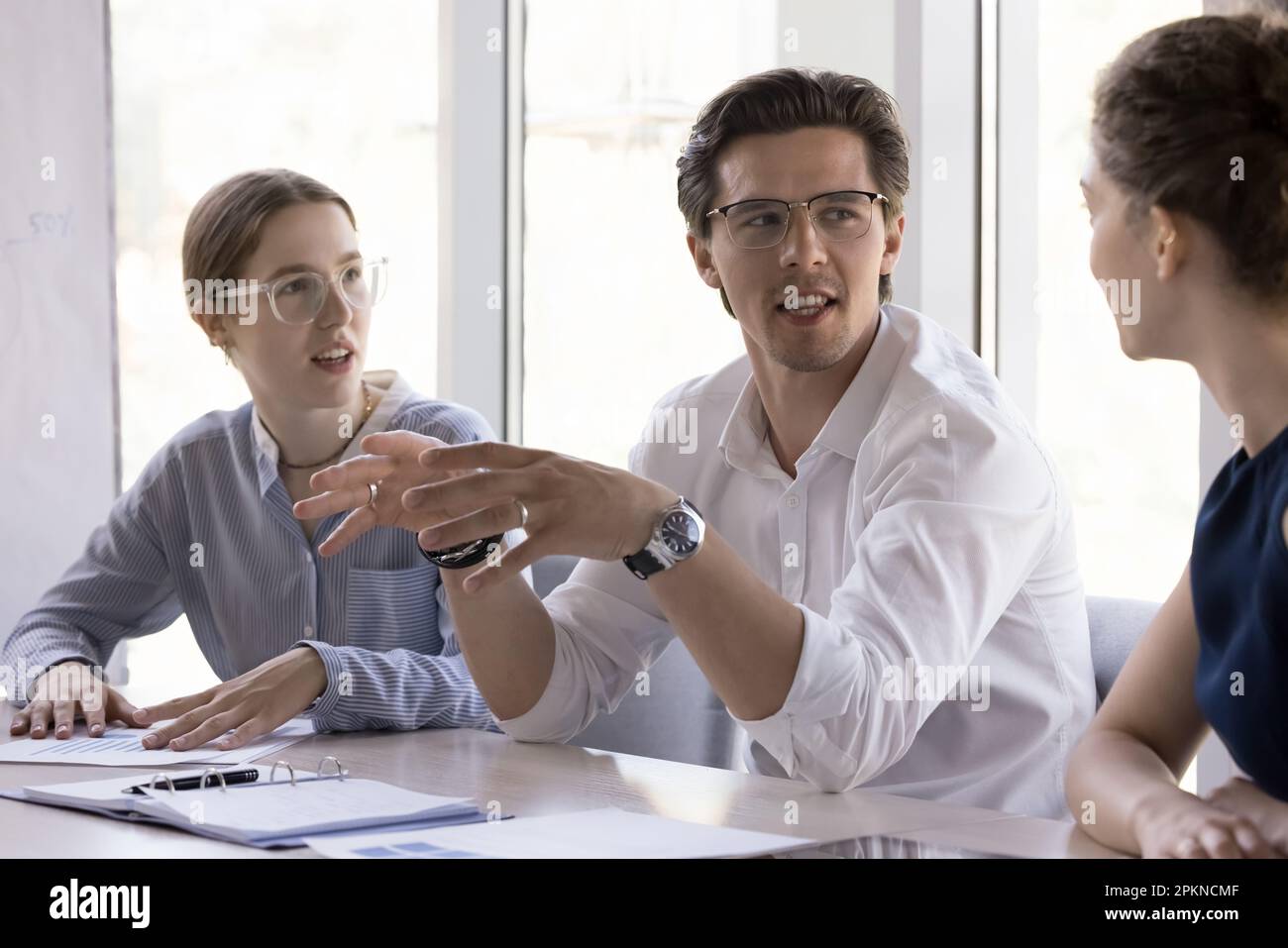 Confident handsome young professional man speaking to female colleagues ...