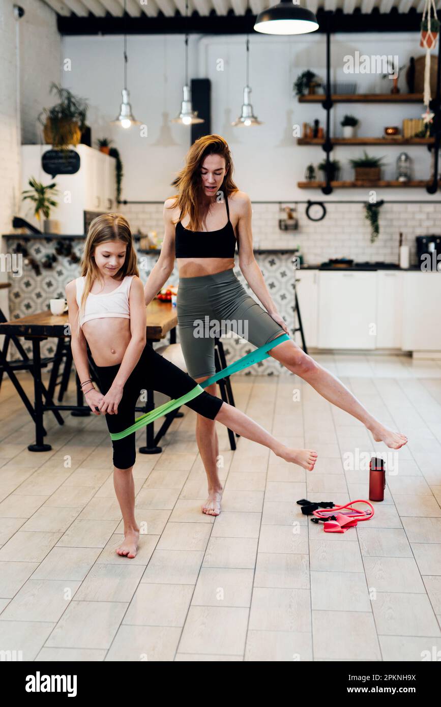 Mother and daughter working out at home doing resistance band leg ...