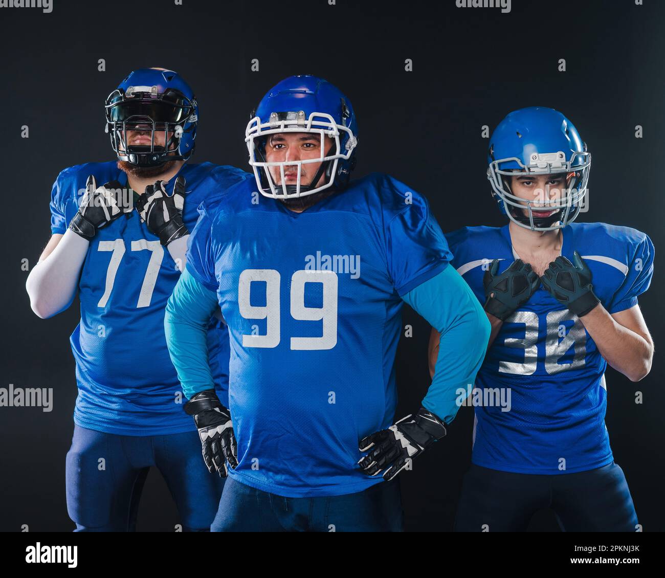 Portrait of three men in blue uniforms for American football on a black ...