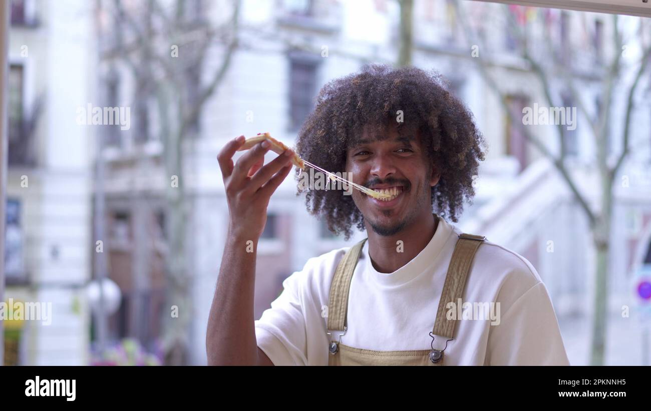 Man with afro hairstyle eating pizza pulling on melted cheese Stock ...