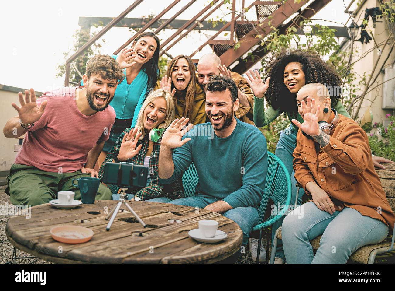 Seven diverse friends sitting around a wooden table on a terrace ...