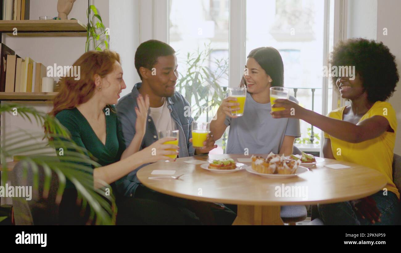 Happy multiethnic friends toasting with juice during breakfast at home ...