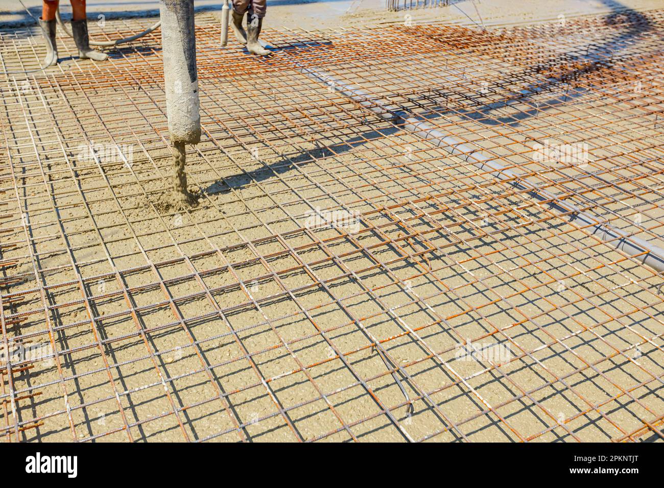 Pump hose is pouring fresh concrete over square reinforcement in the ...