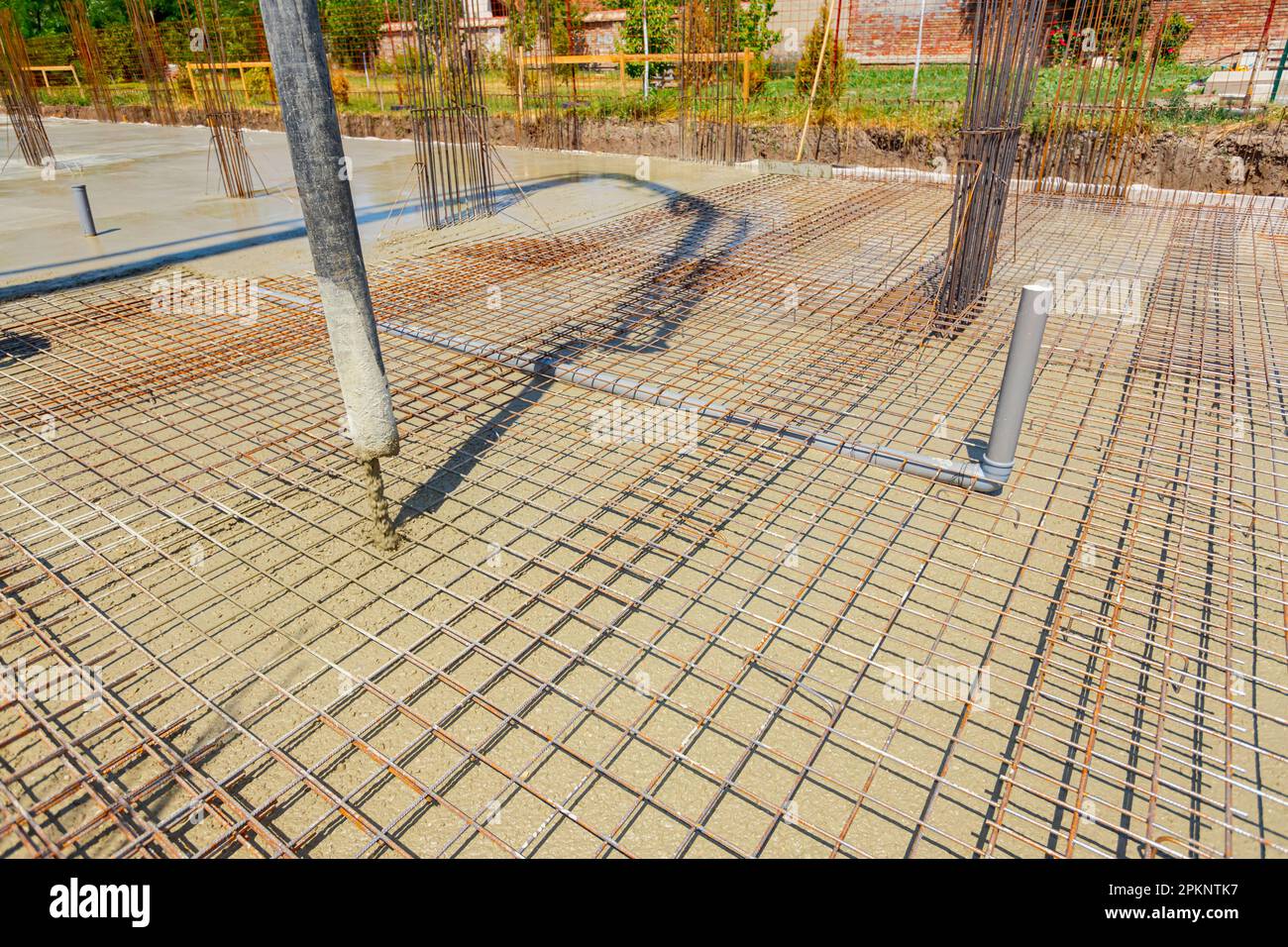 Pump hose is pouring fresh concrete over square reinforcement in the ...