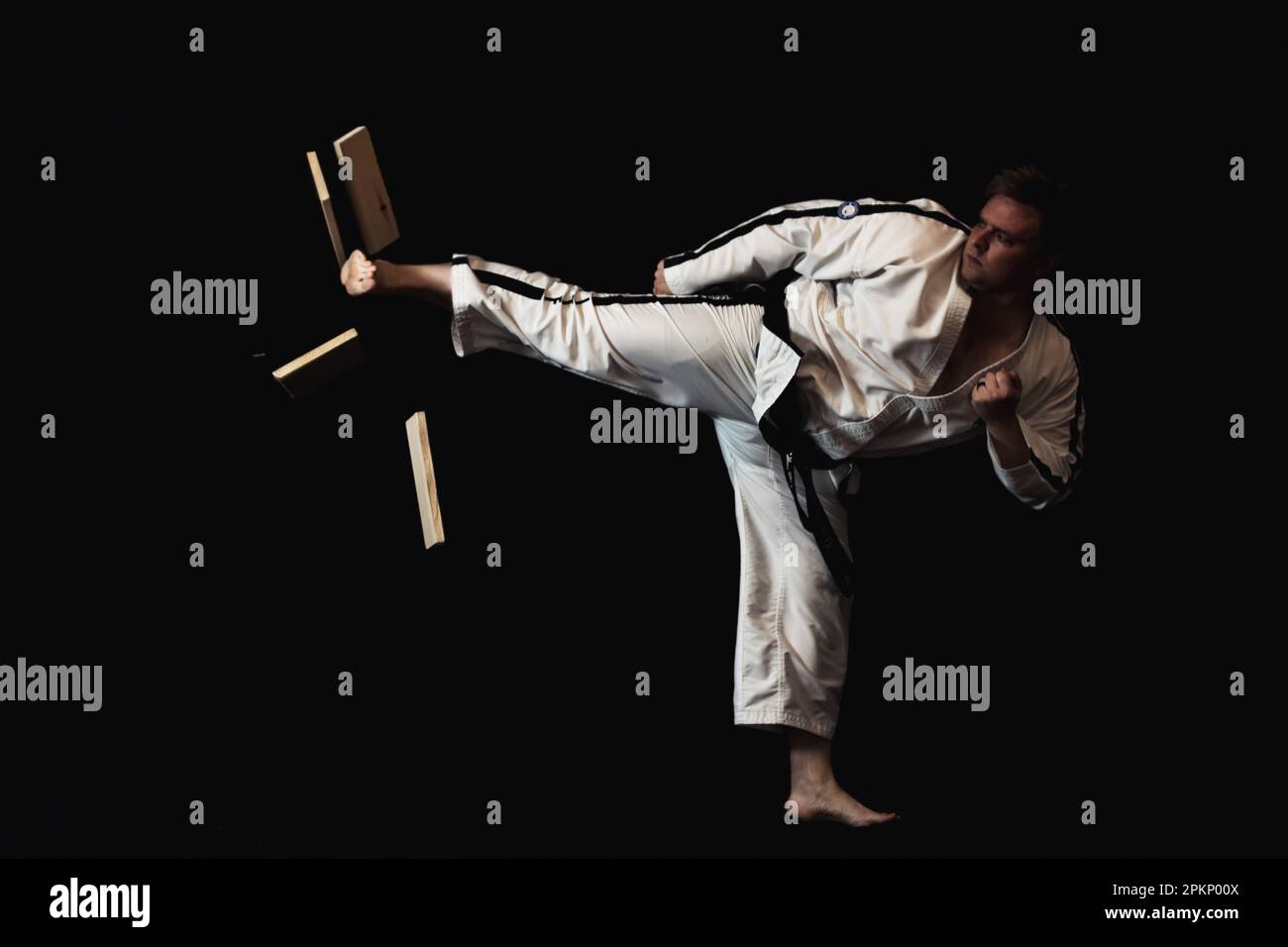 A young man is performing a martial arts maneuver on a solid black ...