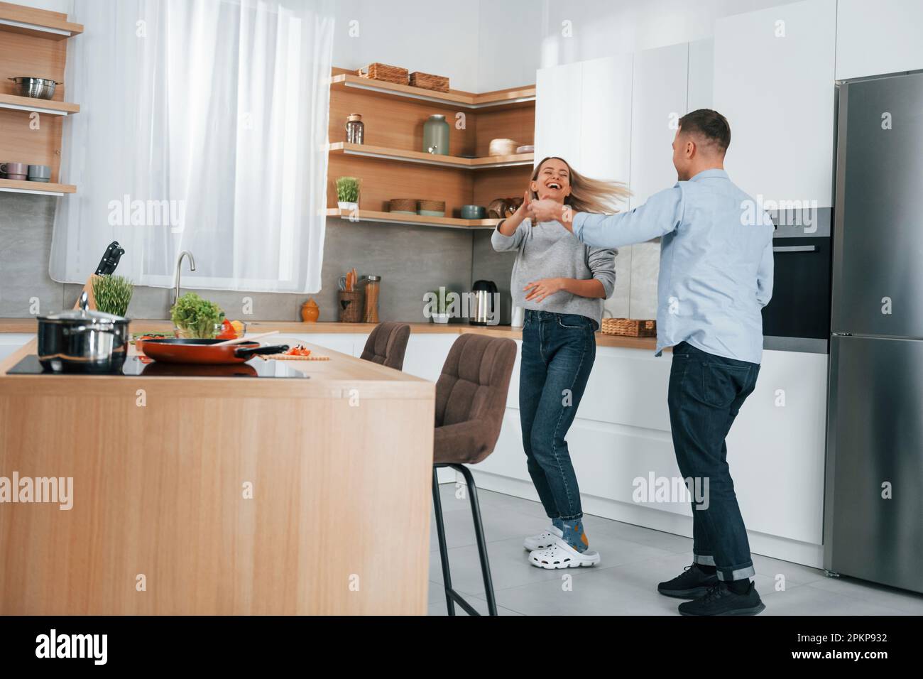 Dancing together. Couple preparing food at home on the modern kitchen ...