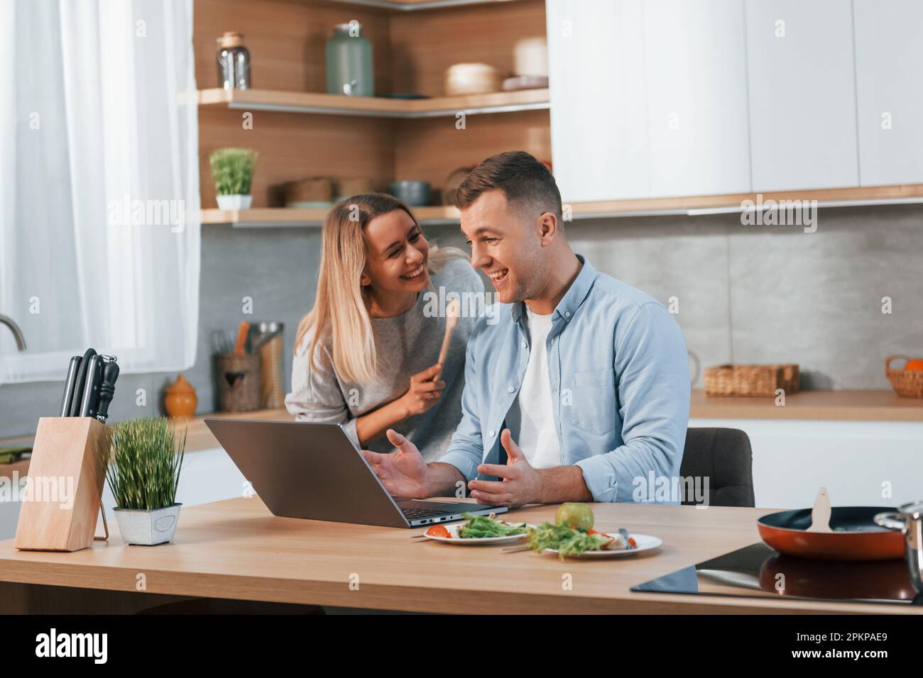 Modern laptop is on the table. Couple preparing food at home on the ...