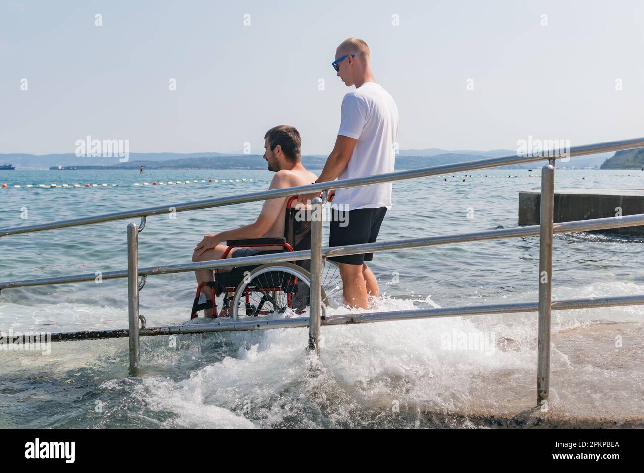 Man with disability at beach goes to swimm on a wheelchair with ...