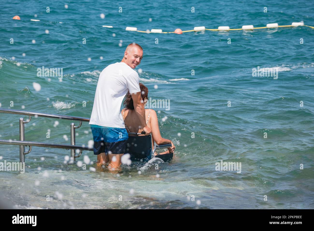 Woman with disability on wheelchair at accessible beach goes swimming ...