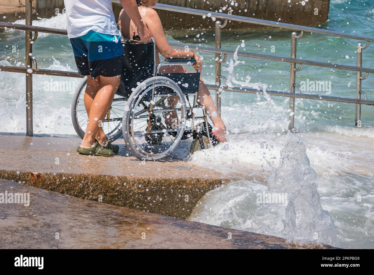Man with disability on wheelchair at accessible beach goes swimming ...