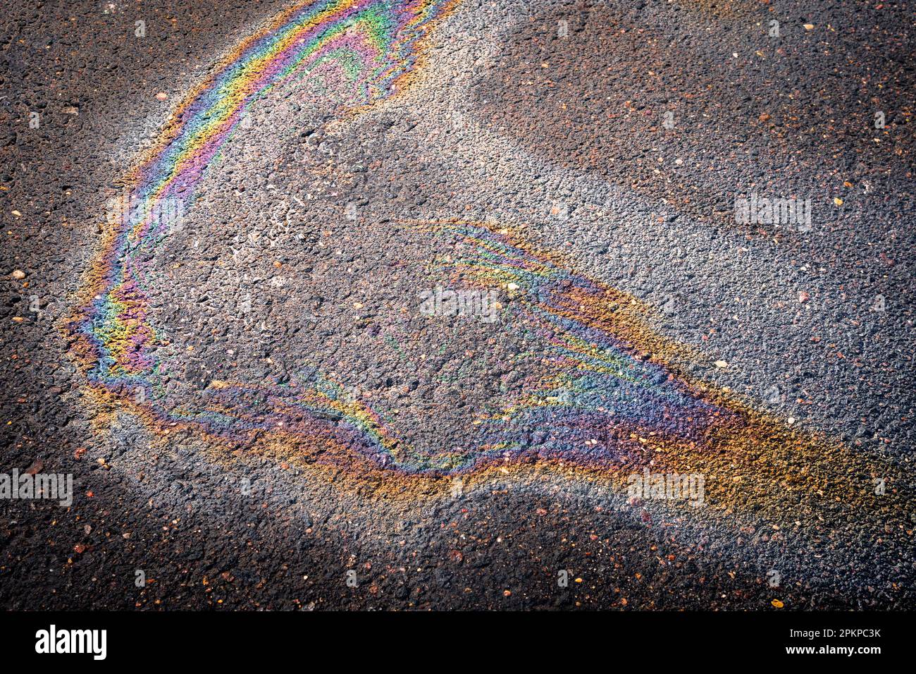 Leakage of oil or gasoline from a car on wet asphalt on a bright sunny ...