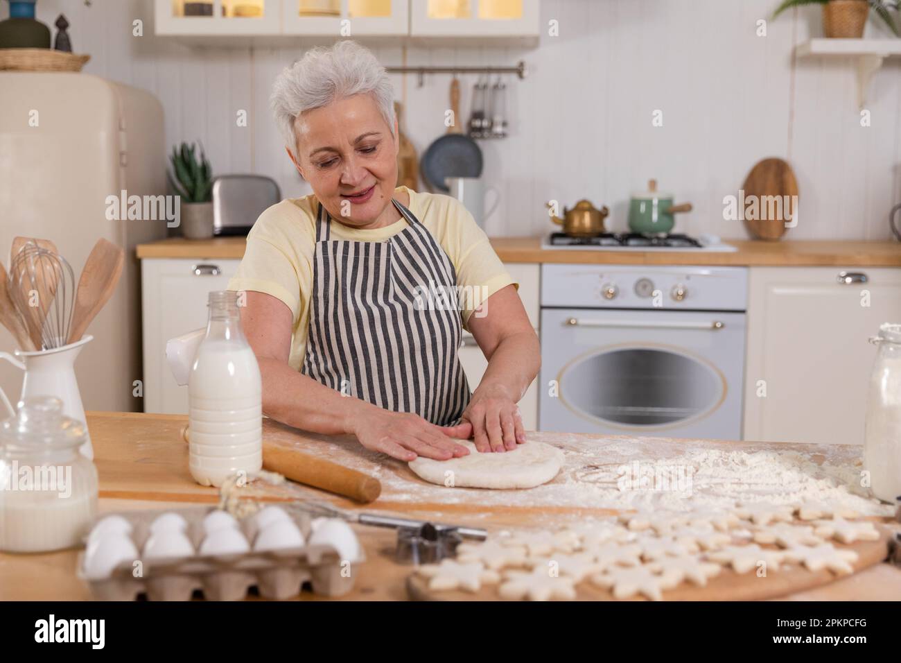 Happy senior woman cooking in kitchen. Stylish older mature gray haired ...