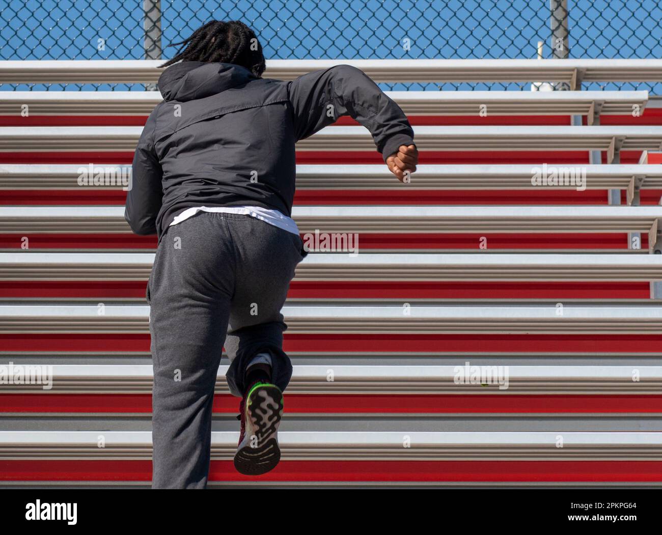 Rear view of a high school boy running up bleachers wearing long black ...