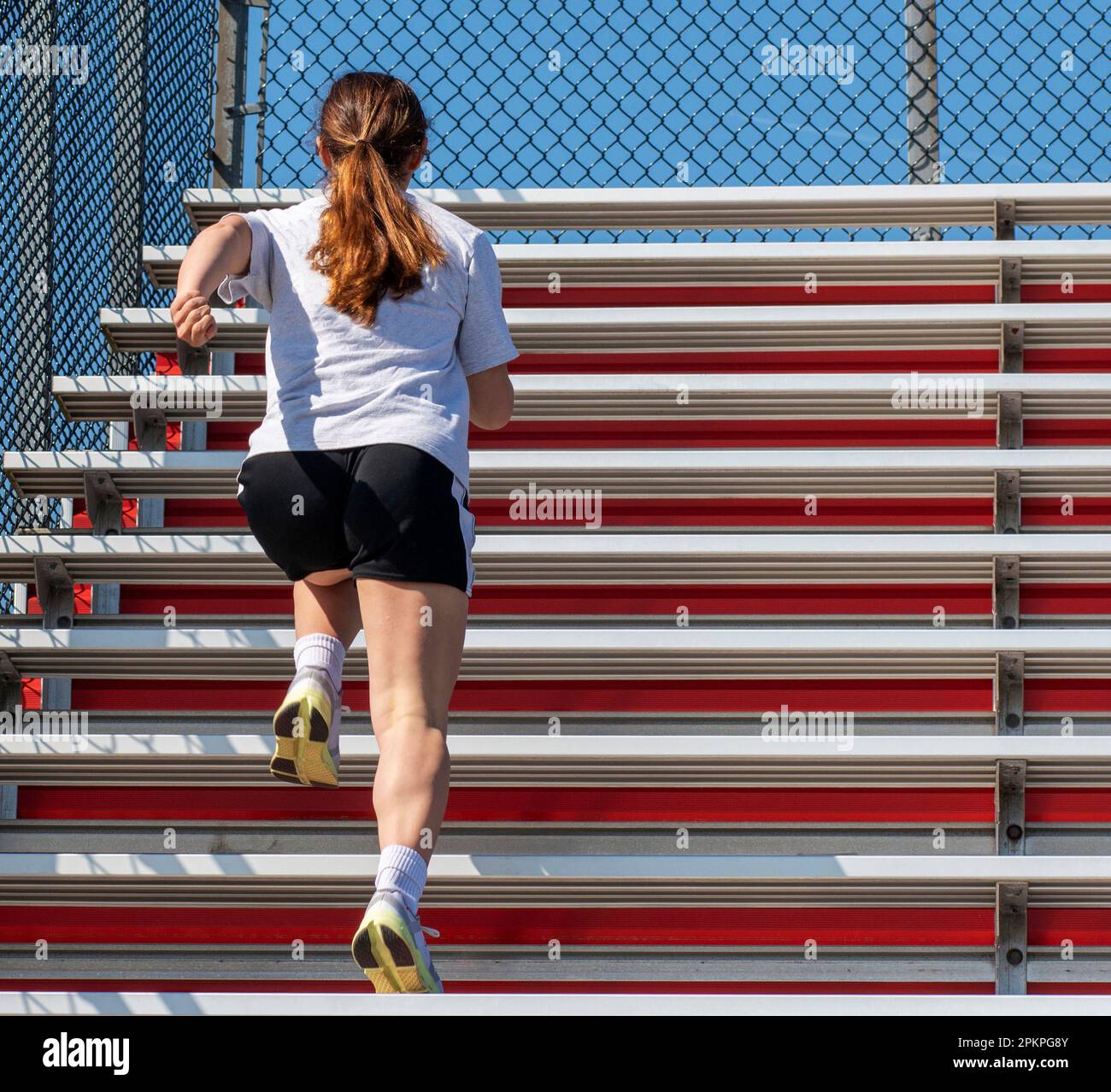 Reav view of a high school girl running up bleacher steps wearing ...