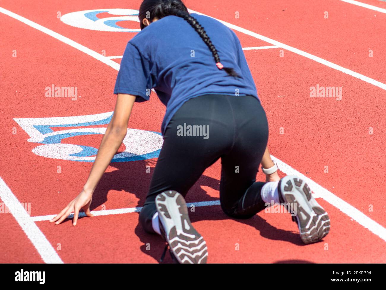 Rear view of a high school girl practicing starting a race in lane five ...