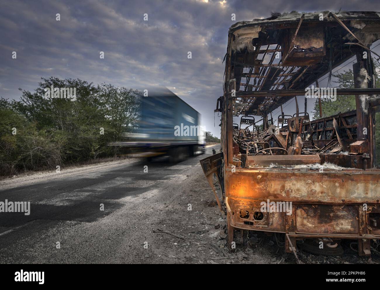 The burnt out wreck of a bus stands on the side of the road between ...