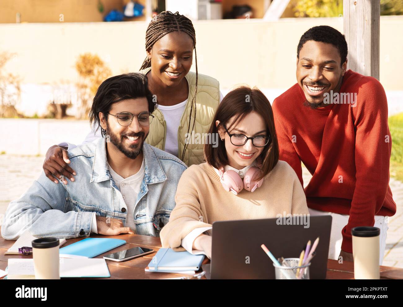 Cheerful millennial multiracial modern students look at computer, have video call, study ...