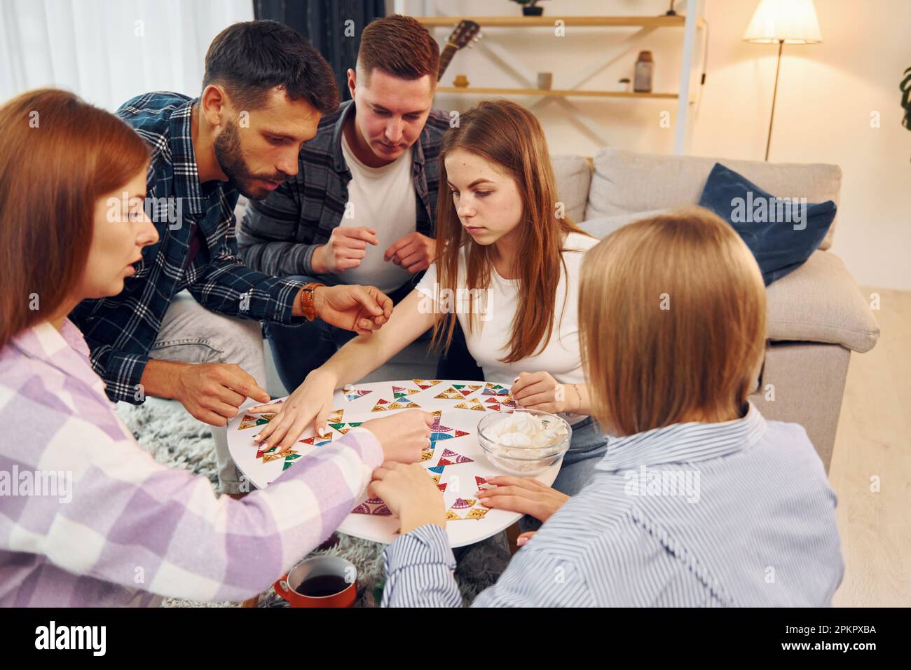 Focused at puzzle game. Group of friends have party indoors together ...