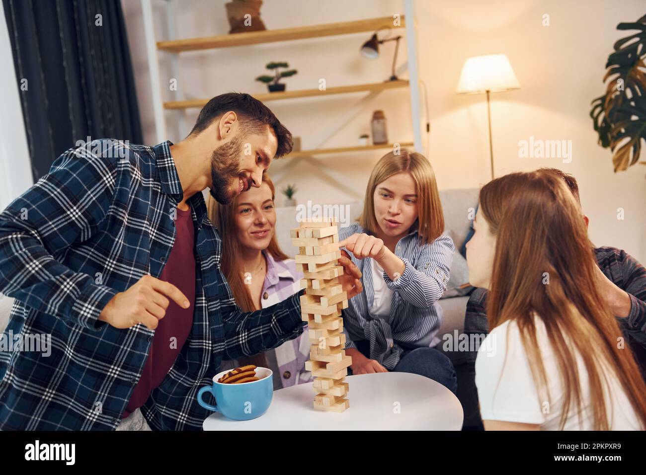 Wooden tower game on the table. Group of friends have party indoors ...