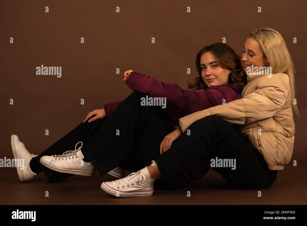 Two beautiful girls in winter jackets sitting on the floor and hugging ...
