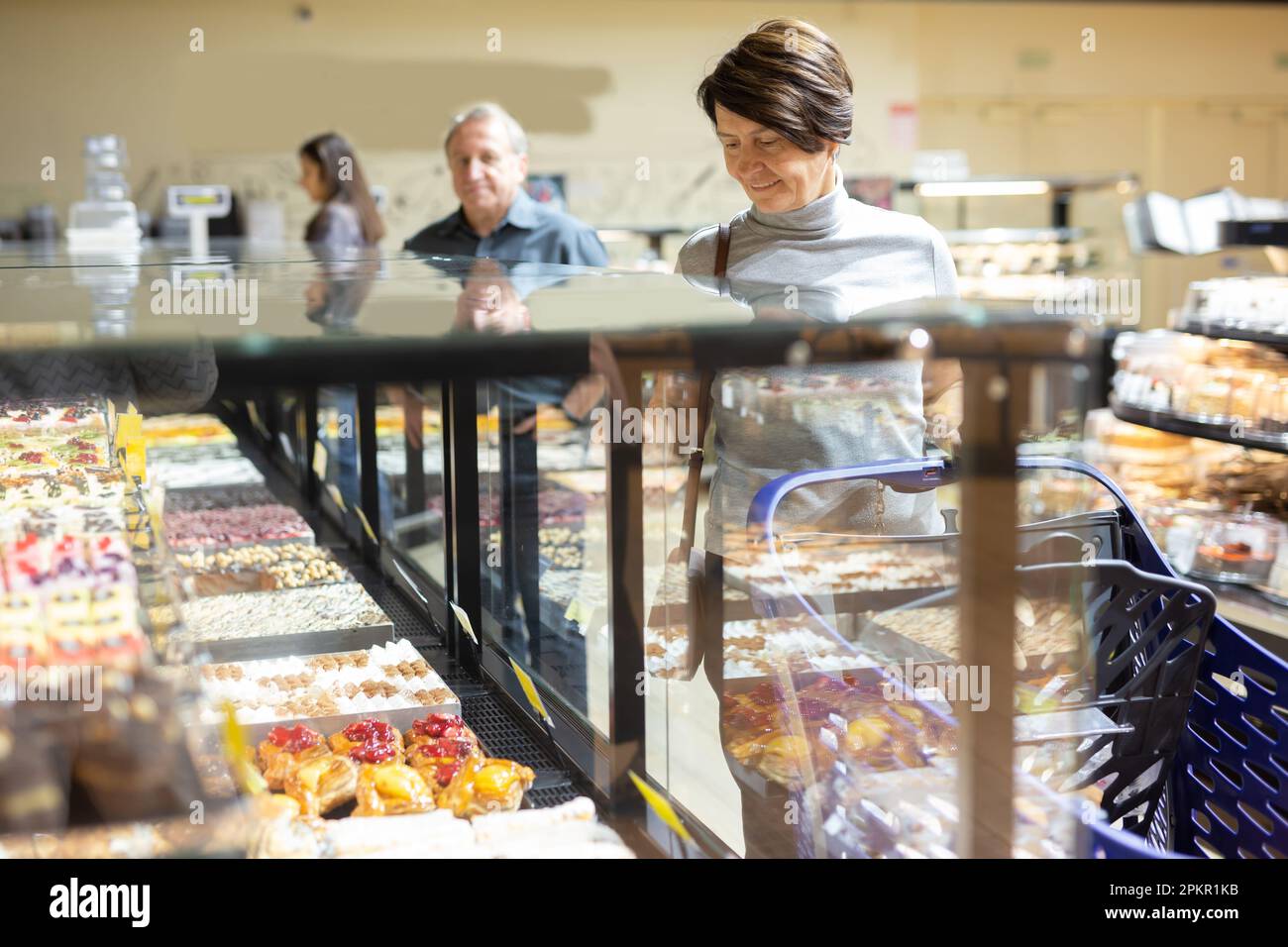 Female customer chooses sweet cakes with interest of the grocery ...