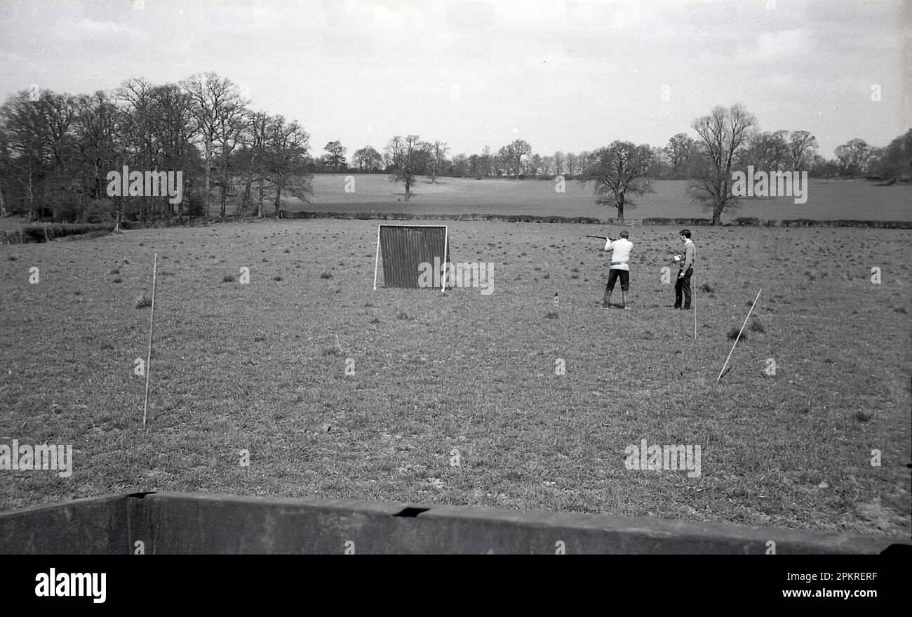 1960s, historical outside in a field, two men with field guns on ...
