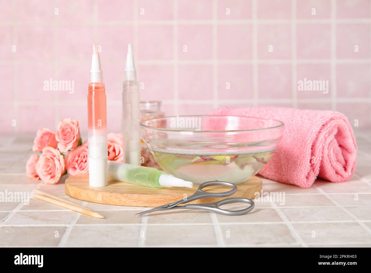 Wooden board with cuticle oil pens, manicure instruments, bowl of water ...