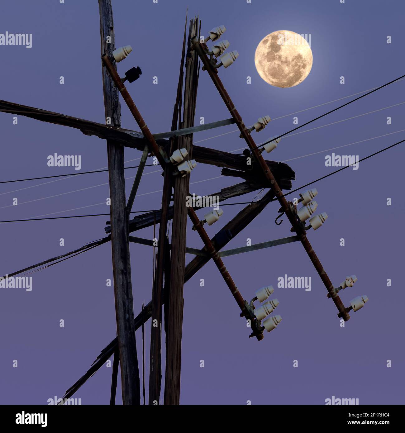 A full moon rises behind some abandoned telephone lines outside ...