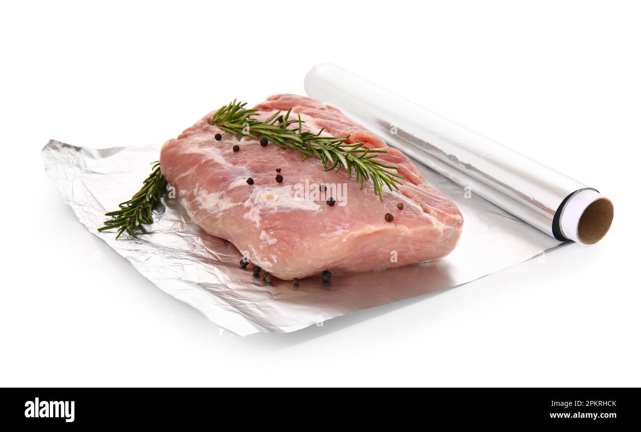 Aluminium foil roll with piece of raw meat, rosemary and peppercorns on ...