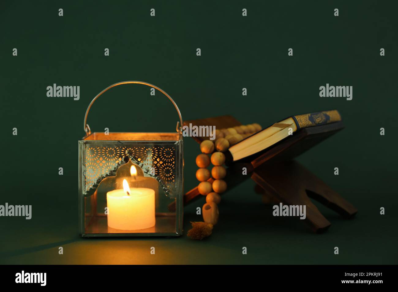 Muslim lamp with burning candle, Koran and prayer beads on dark green ...