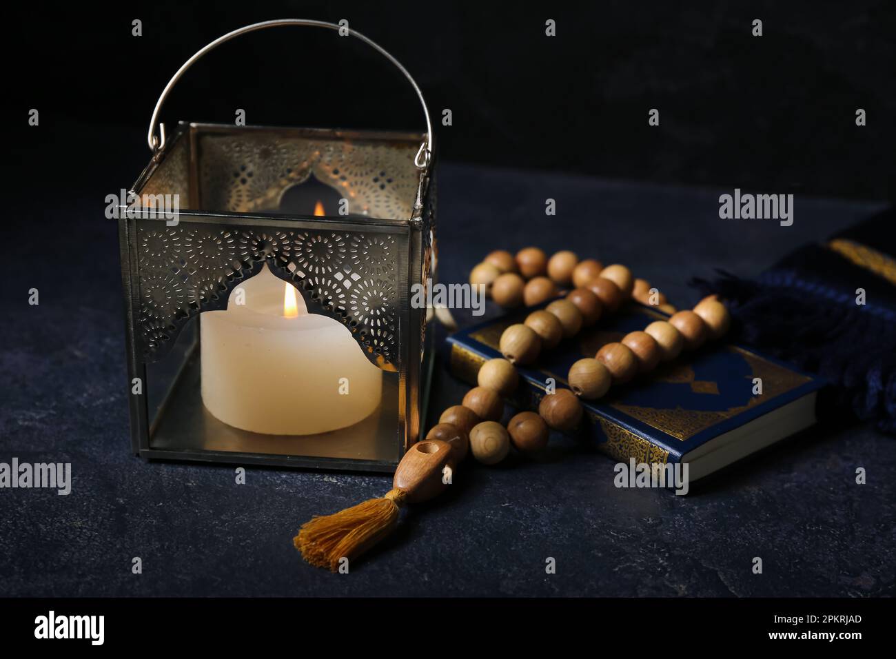 Muslim lamp with burning candle, prayer beads and Koran on dark ...