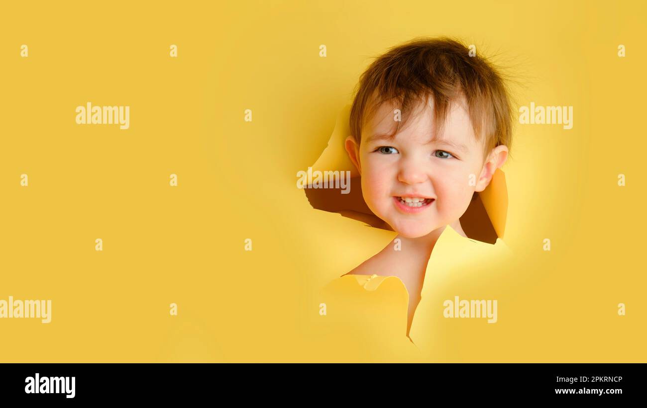 A sly baby in a hole on a paper yellow background. Torn child's head ...