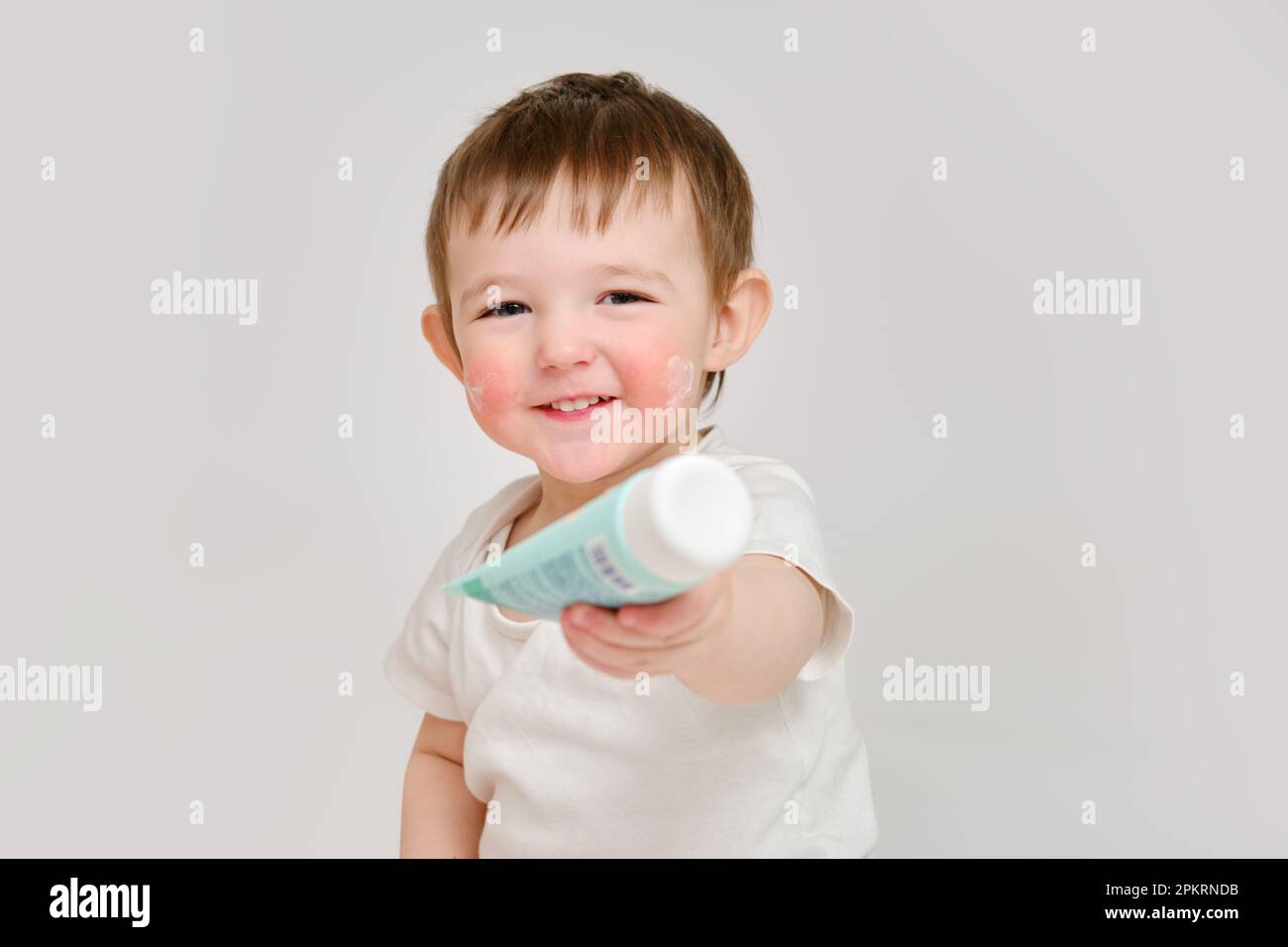 Happy baby holding a tube of cream on a studio white background ...
