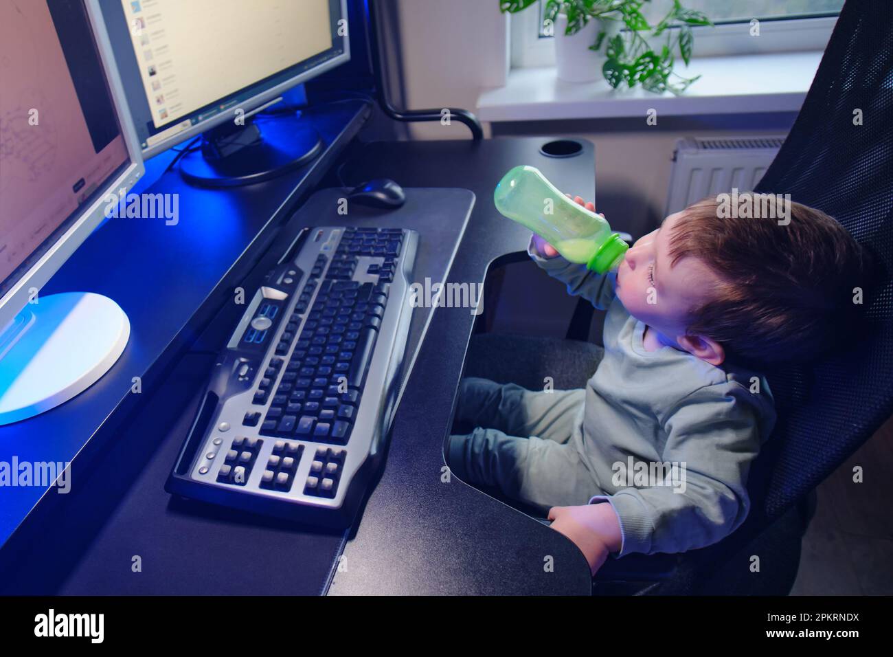 Happy baby is sitting at the computer keyboard with a bottle of milk in ...