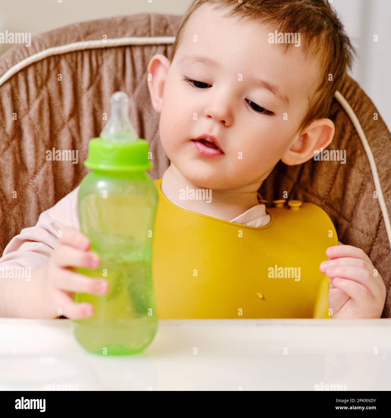 Happy toddler baby drinking from a bottle while sitting on a high chair ...
