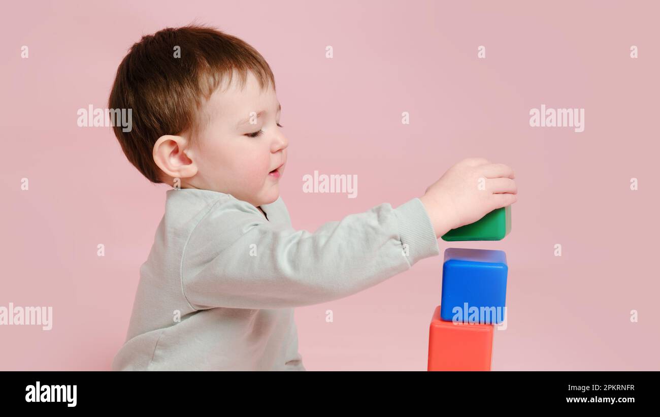 Happy toddler baby plays with cubes on studio pink background. Child ...