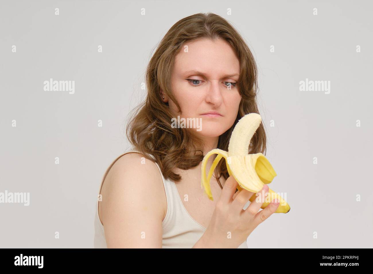 A woman with doubt and contempt looks at a banana, a studio white ...