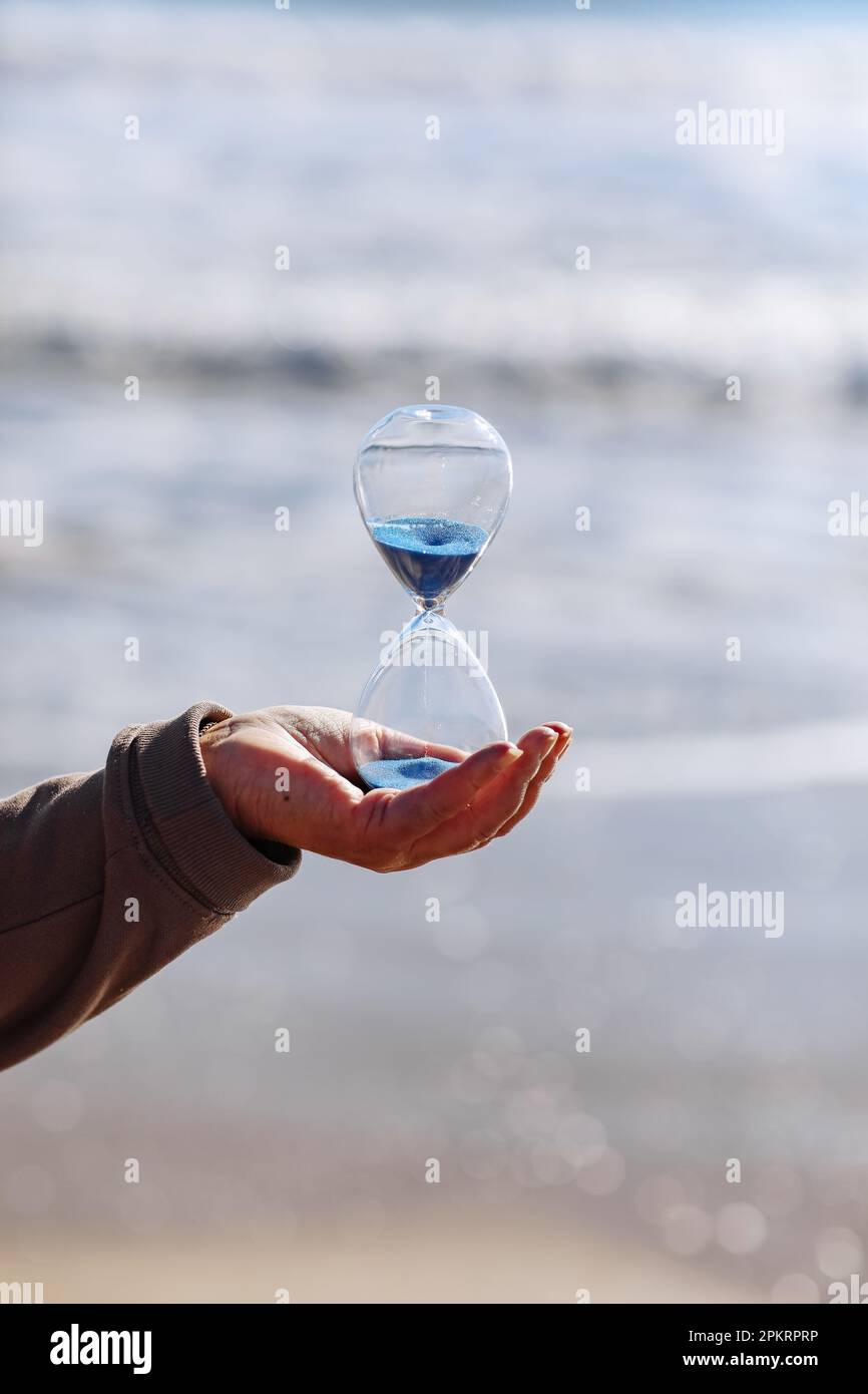 Time is running fast. Hourglass with blue sand inside in mature woman's ...
