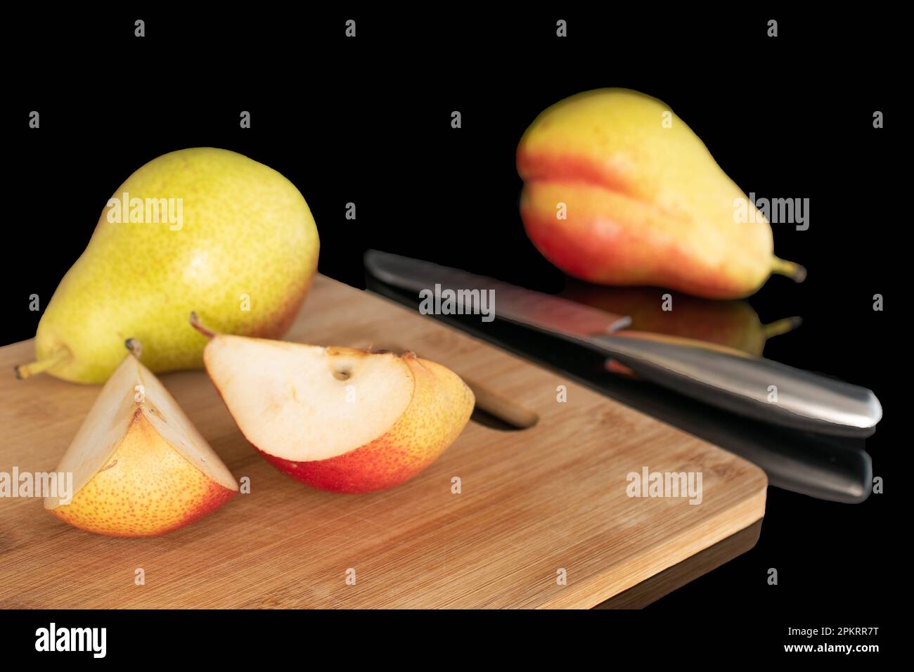 Whole pears and slices on a wooden board with a knife, close-up, on a ...