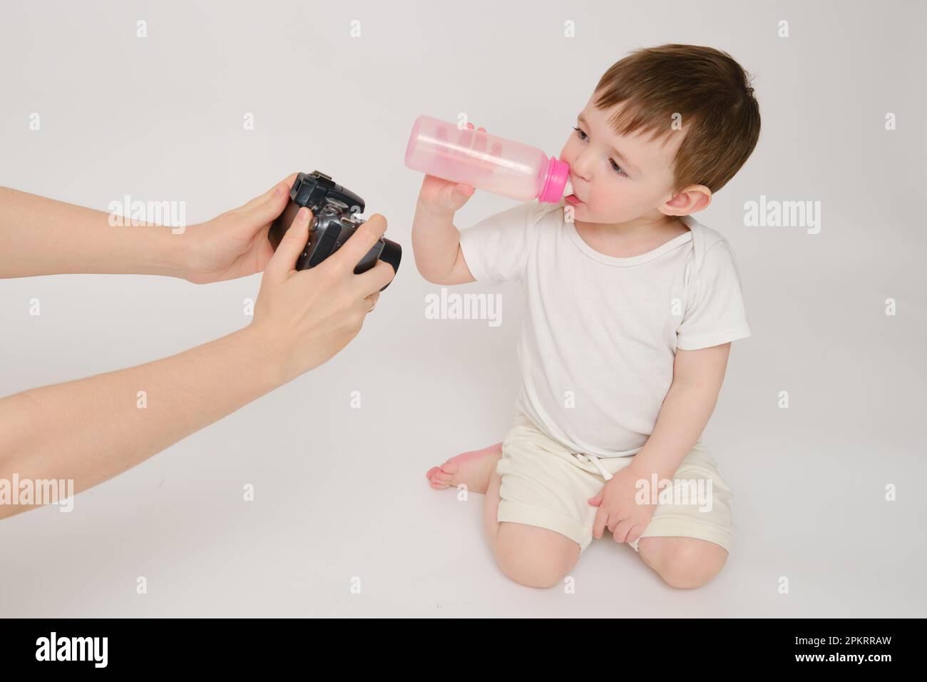 Woman mother photographs baby on photo camera, studio white background ...