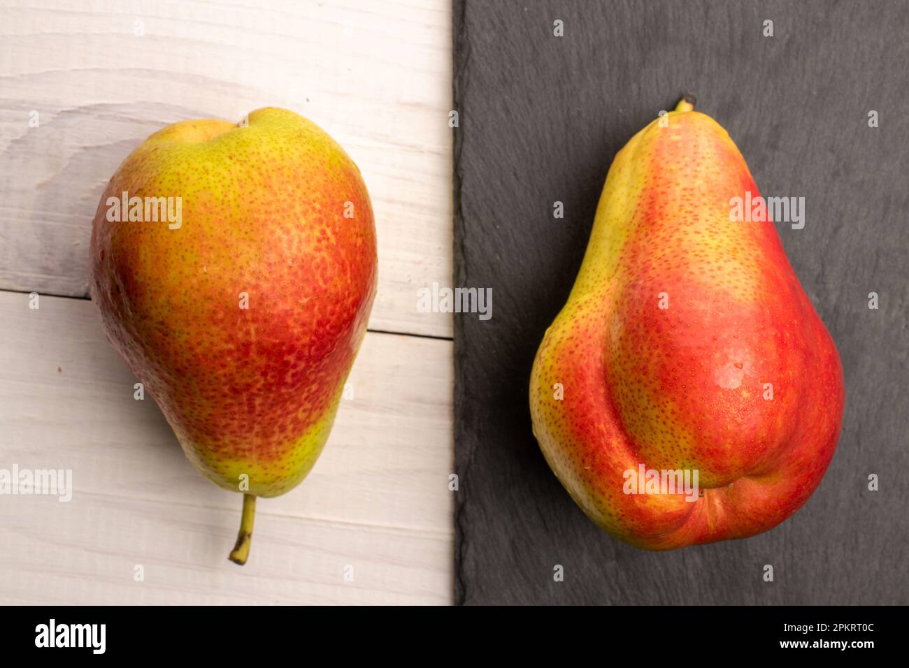Two flavorful pears on a slate board and white wooden table, top view ...