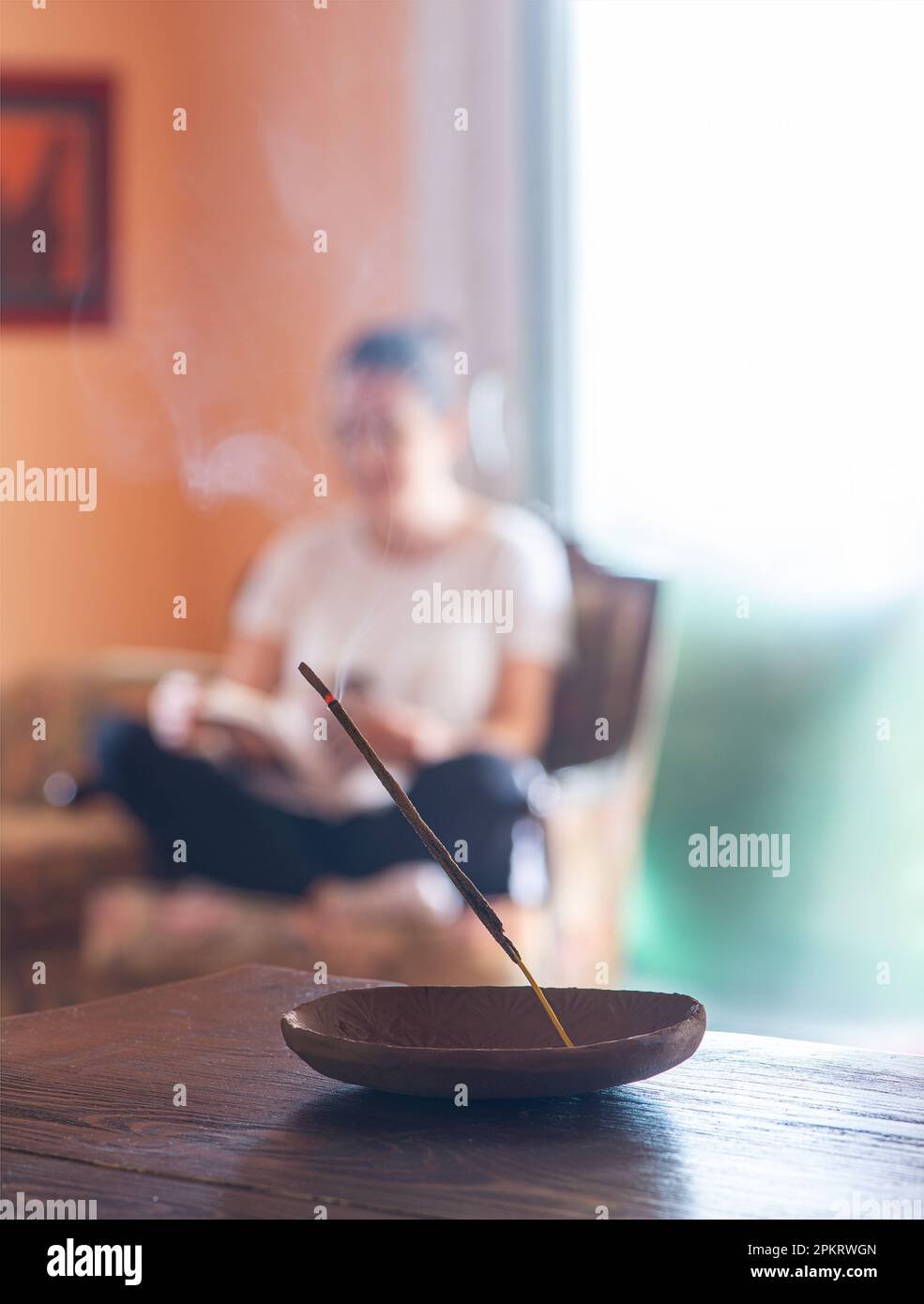Incense stick burning with a woman sitting crosslegged reading a book ...