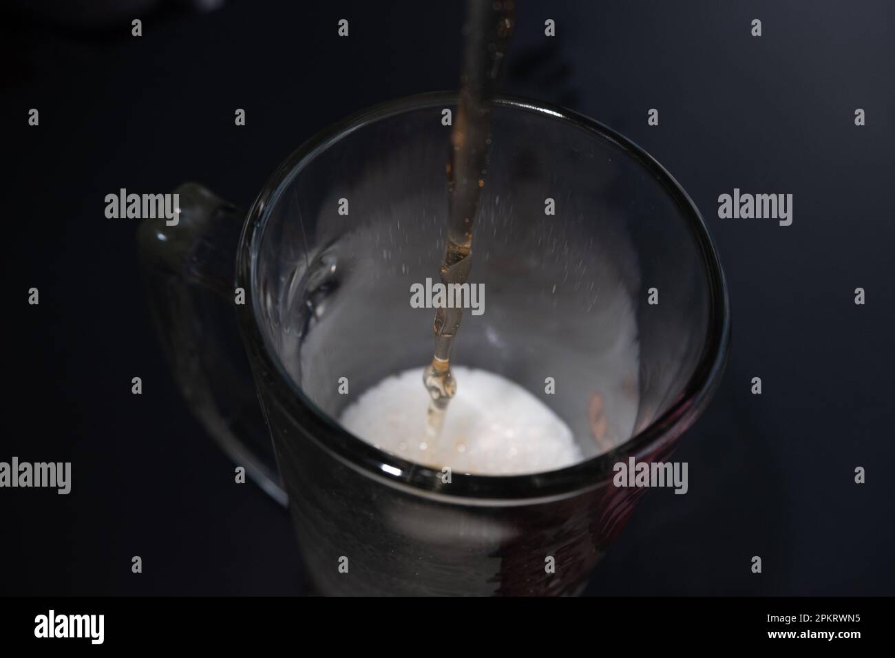 A stream of beer pours into a glass. Dark background Stock Photo - Alamy
