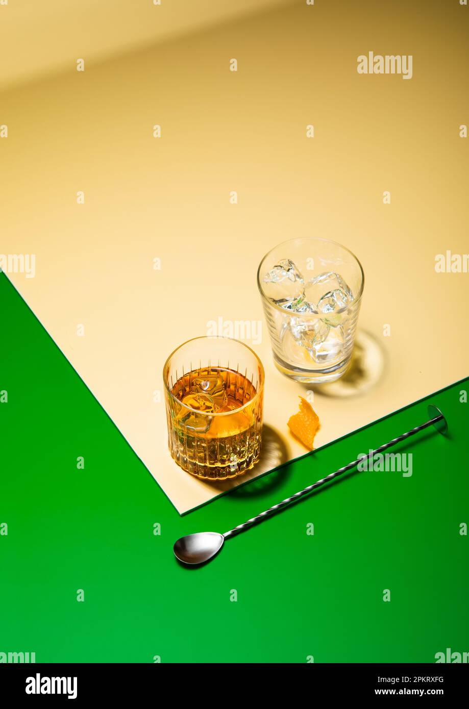 Whiskey glass with bar spoon and empty glass with ice cubes on gre ...