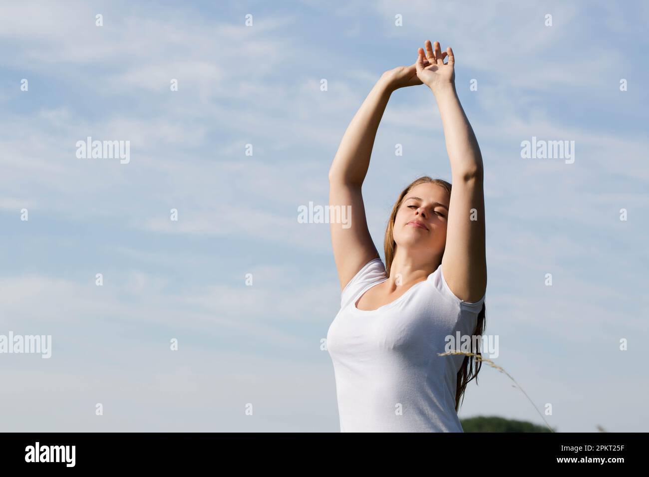 Happy, free woman standing with arms raised, saluting the sun outdoors ...