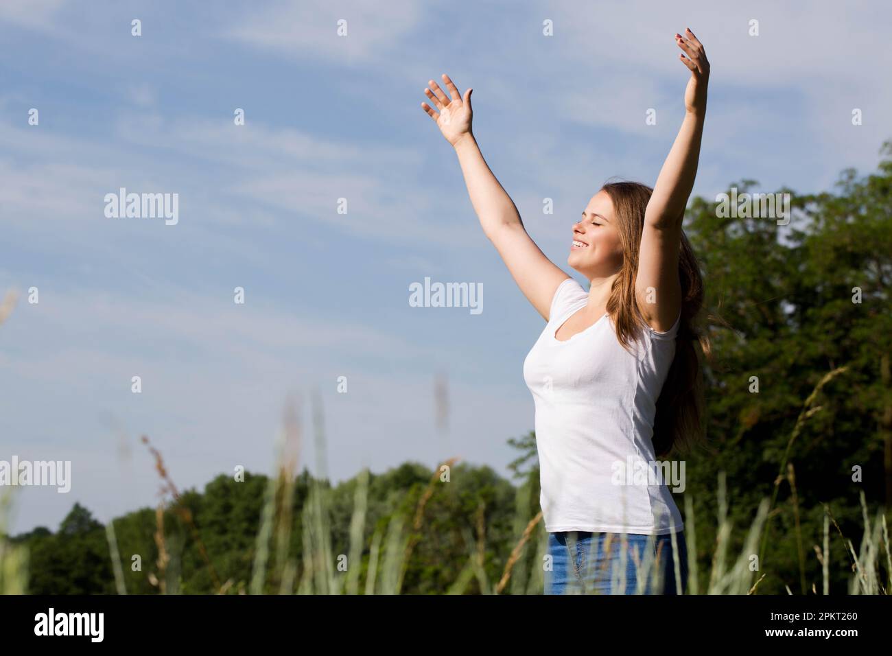 Happy, free woman standing with arms raised, saluting the sun outdoors ...