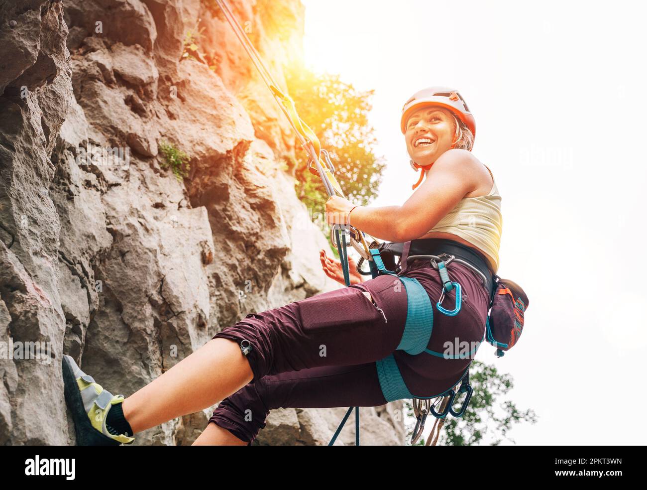 Smiling athletic woman in protective helmet and shoes climbing cliff ...