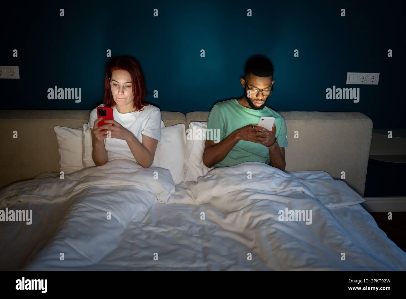 Young multiracial couple lying in bed using smartphones not talking ...
