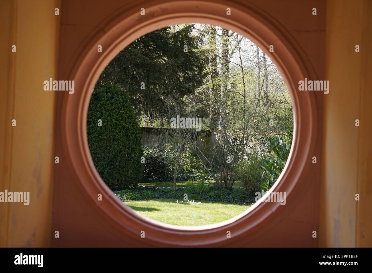 An oval window view of the outside of a house, with a lush green tree ...